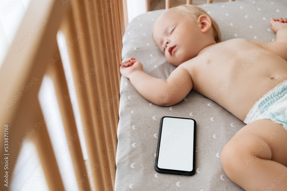 Little baby in diaper napping safely in bed with phone playing music in ...