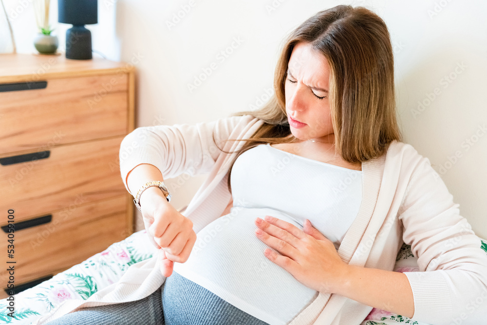 Pregnant contractions time. Pregnancy woman watching clock, holding ...