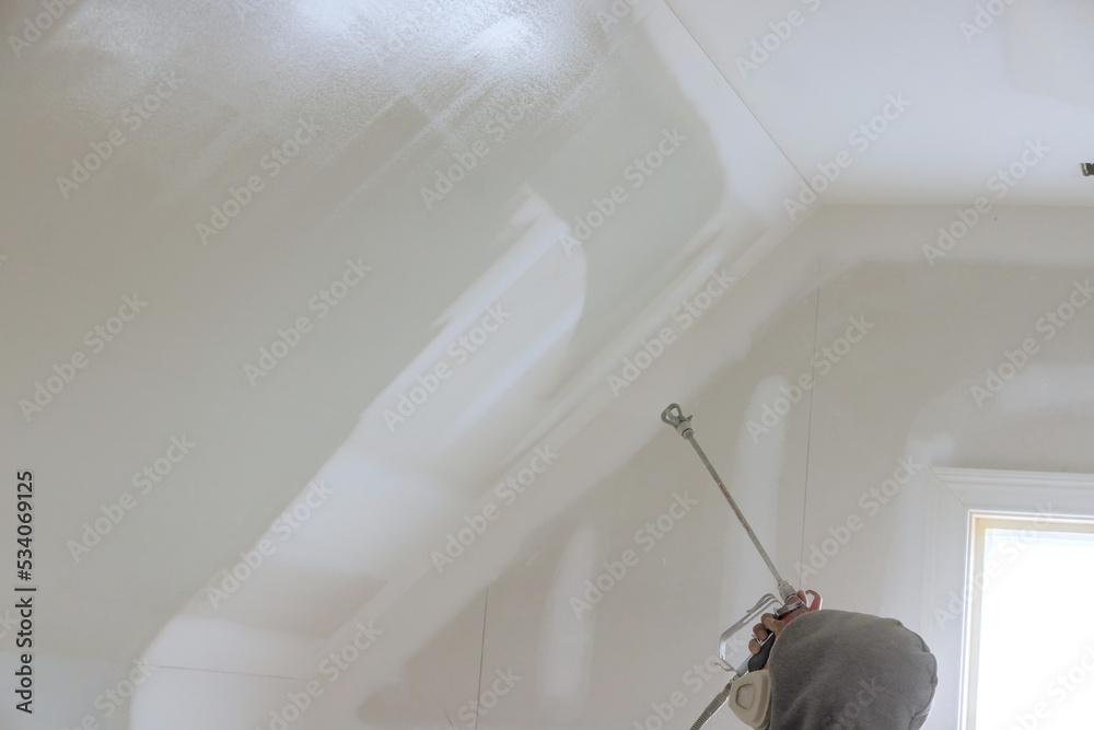 Using a spray gun and a primer, the worker paints the walls and ...