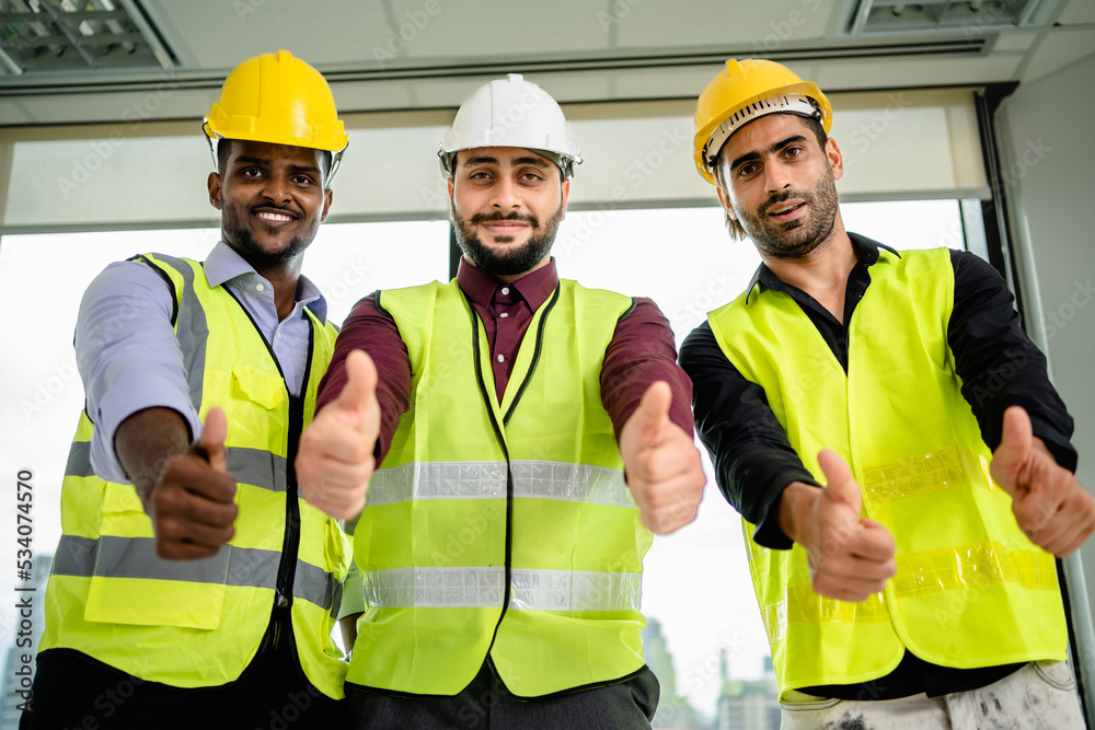 A team of happy engineers diverse shows thumbs up together looking at ...