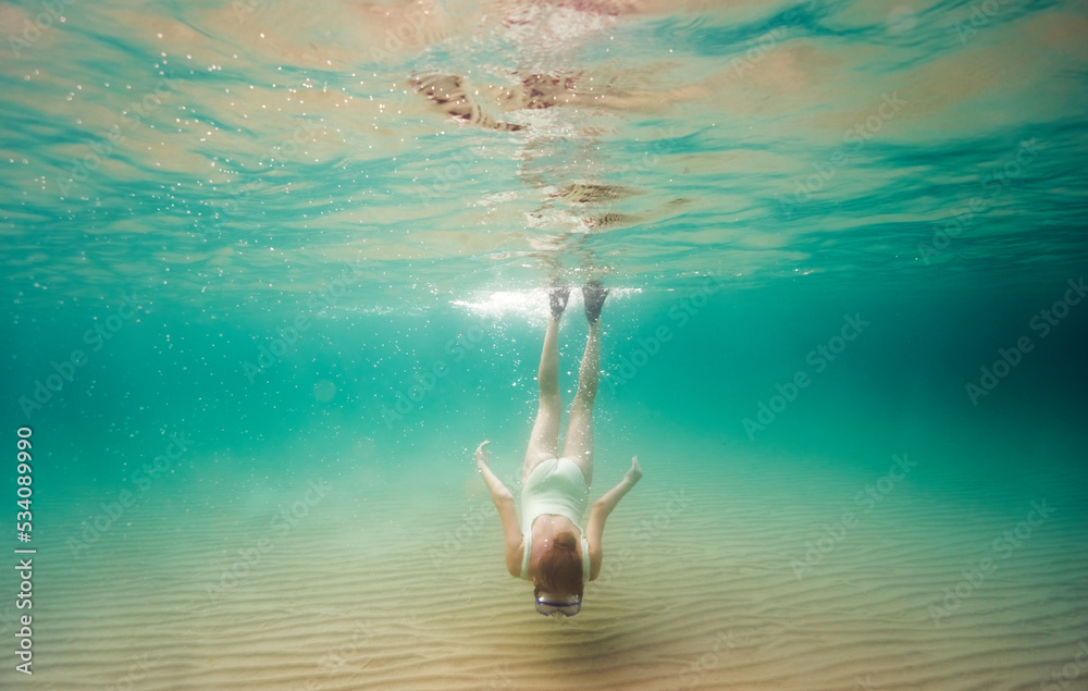 A Teenage Girl In An Underwater Mask Dives To The Sandy Bottom At A