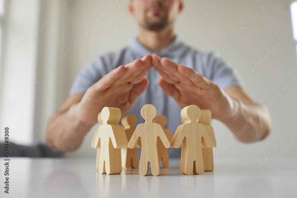 Young man holding hands above small wooden toy human figures placed on ...