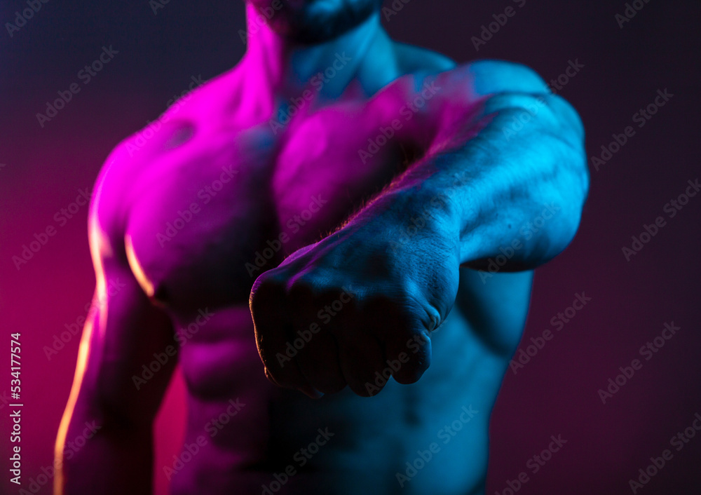 Foto de Sportive man bodybuilder shows fist in the colorful neon light ...