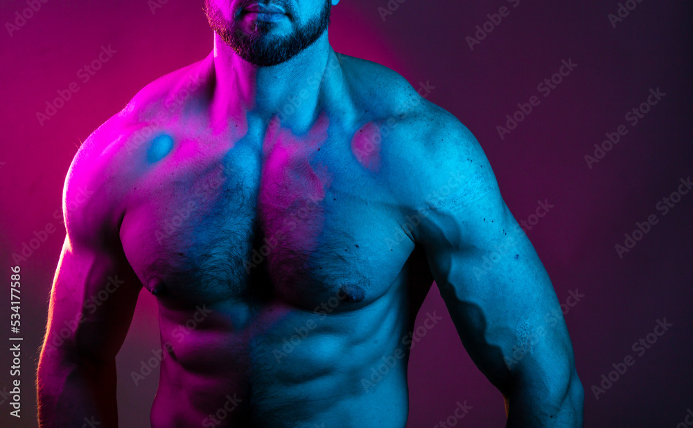 Sportive man bodybuilder is posing in the colorful neon light with ...