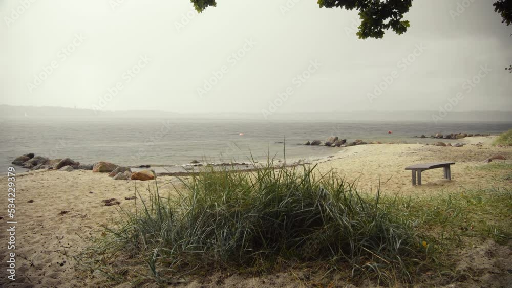 Empty beach with dune grass and wooden bank in the front on a overcast ...