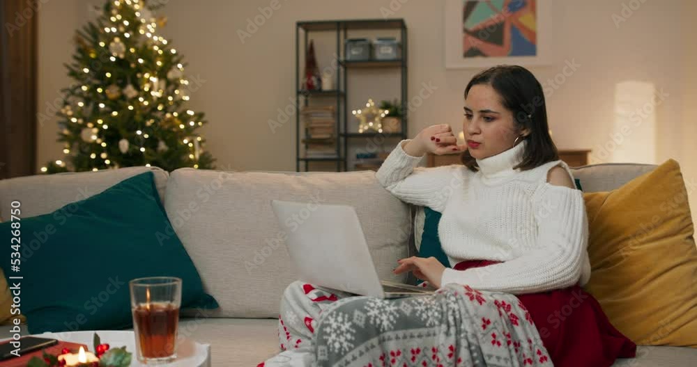 Young woman working from home remotely on laptop on Christmas Day sits ...