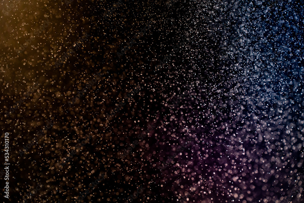 Dust particles floating on a colorful rainbow light on black background ...