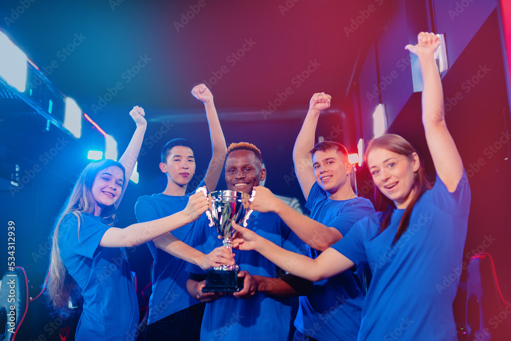 Multi cultural team winner of video games tournament. Holding big cup ...