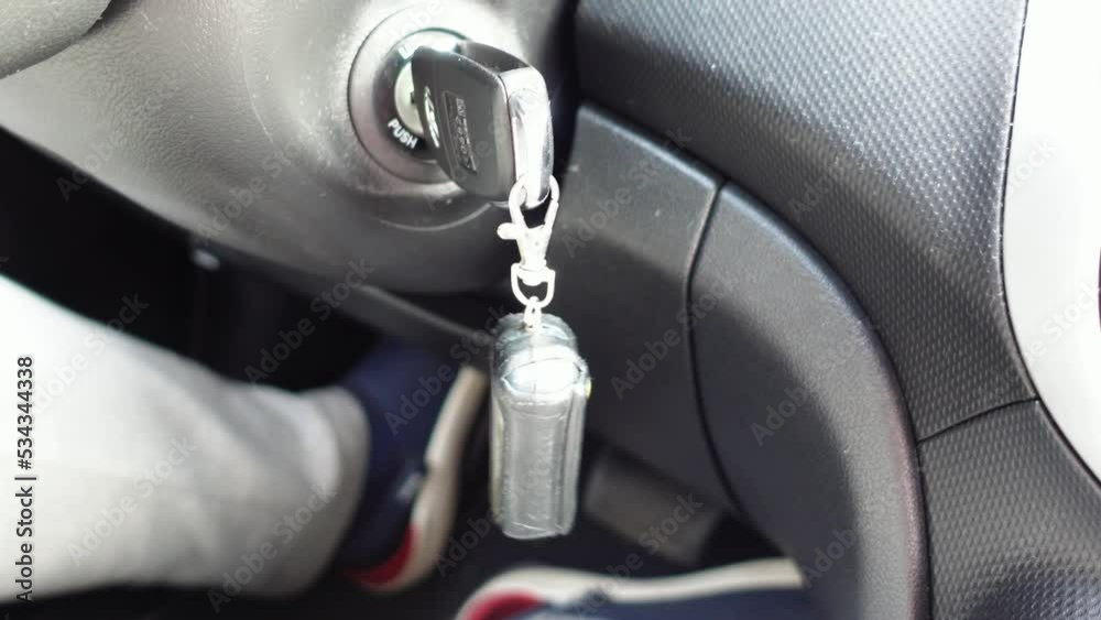 Key inserted into ignition lock of car. Male person foot presses on ...