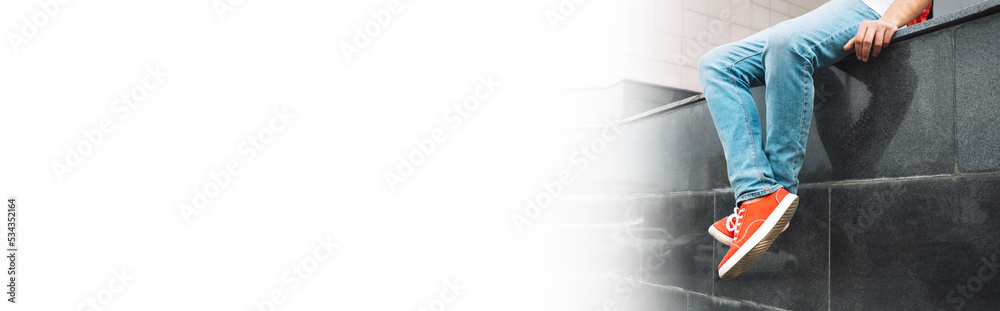 Men's legs in jeans and red sneakers. student sits on the parapet ...