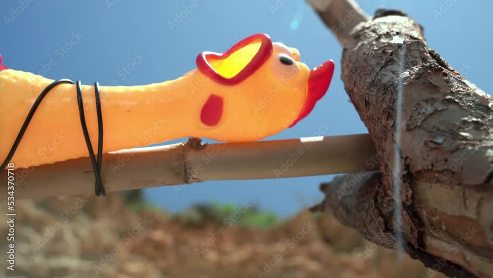 Yellow plastic chicken spinning on spit blue sky and sun glare, bottom ...