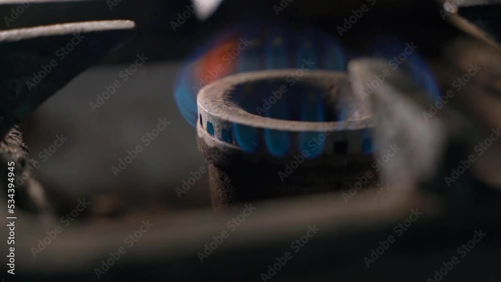 Blue fuel burns in the burner of an old untidy kitchen stove close-up ...