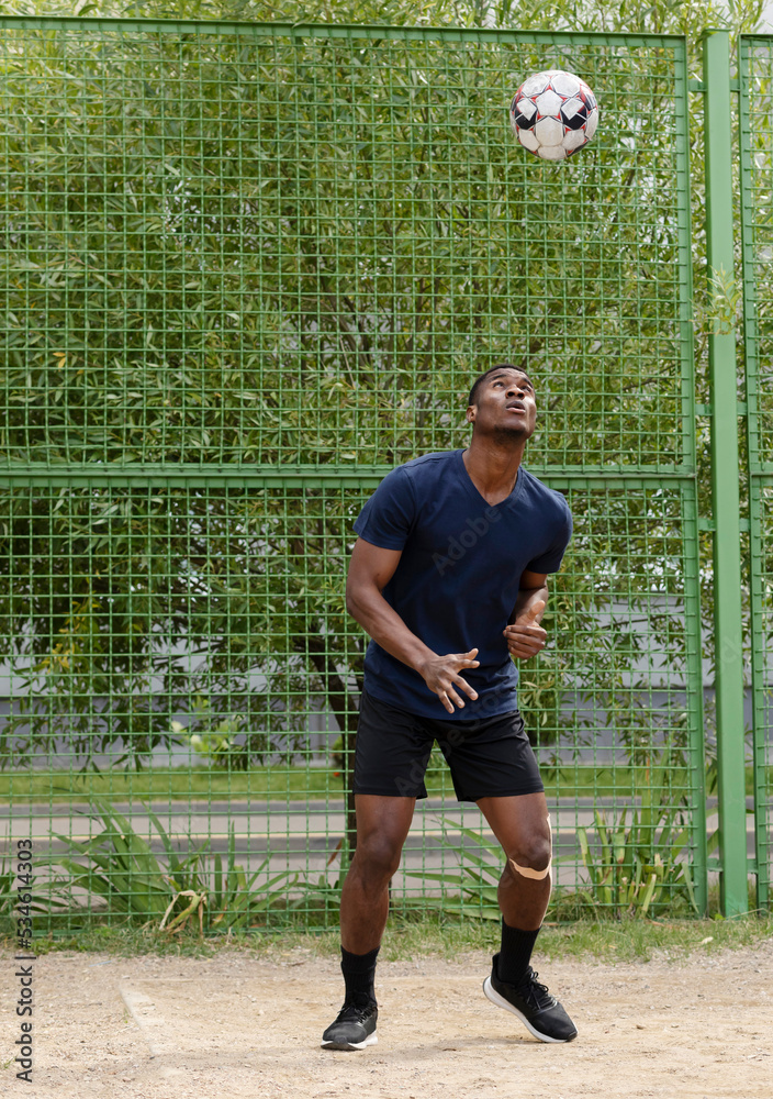 Young confident african american guy with taped knee kicks soccer ball ...