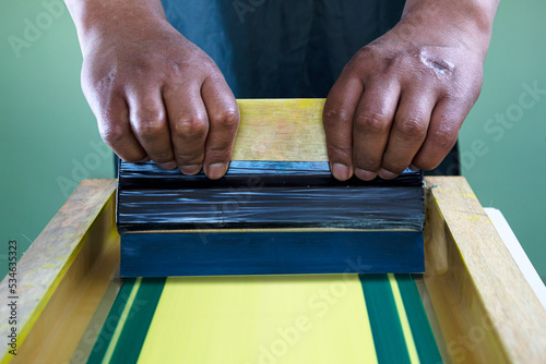 The man's hands perform the screen printing work, on the work table ...