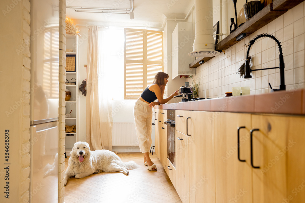 Woman makes coffee while standing with her dog in kitchen. Interior of ...