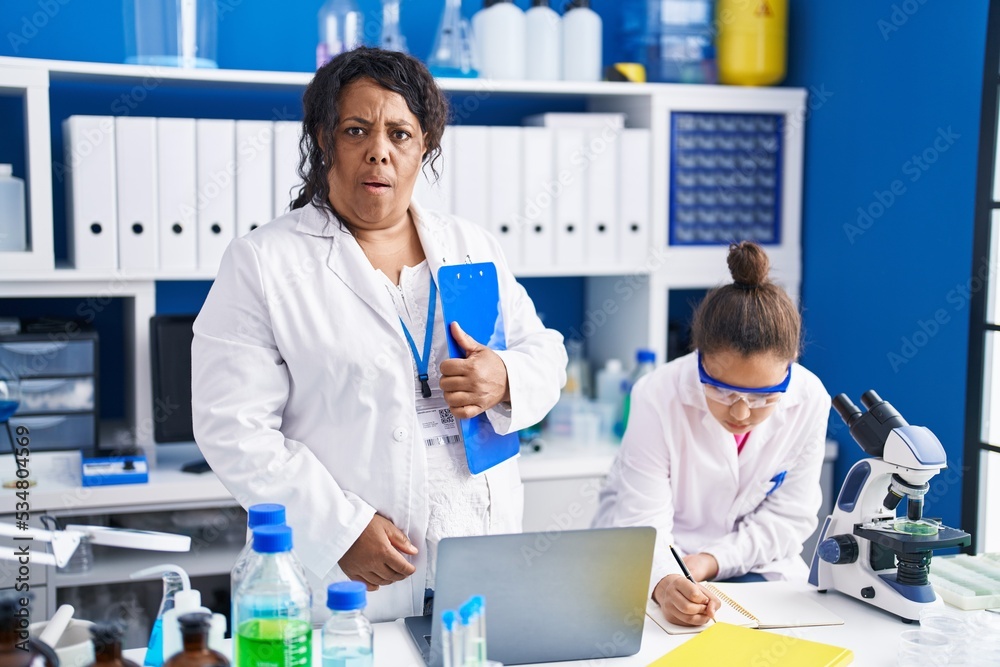 Mother and young daughter working at scientist laboratory scared and ...