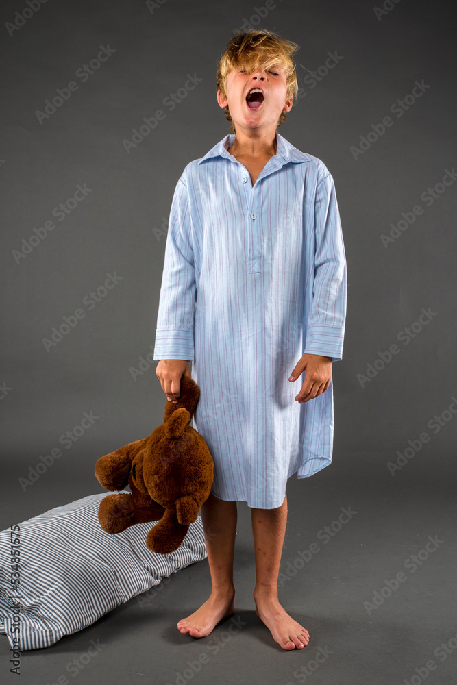 Cute little boy in a nightshirt yawning while holding his stuffed bear ...