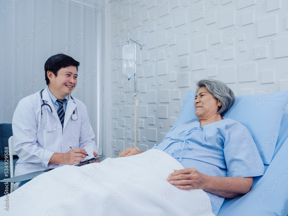 Smiling Asian doctor in white suit take notes while discussing happy ...