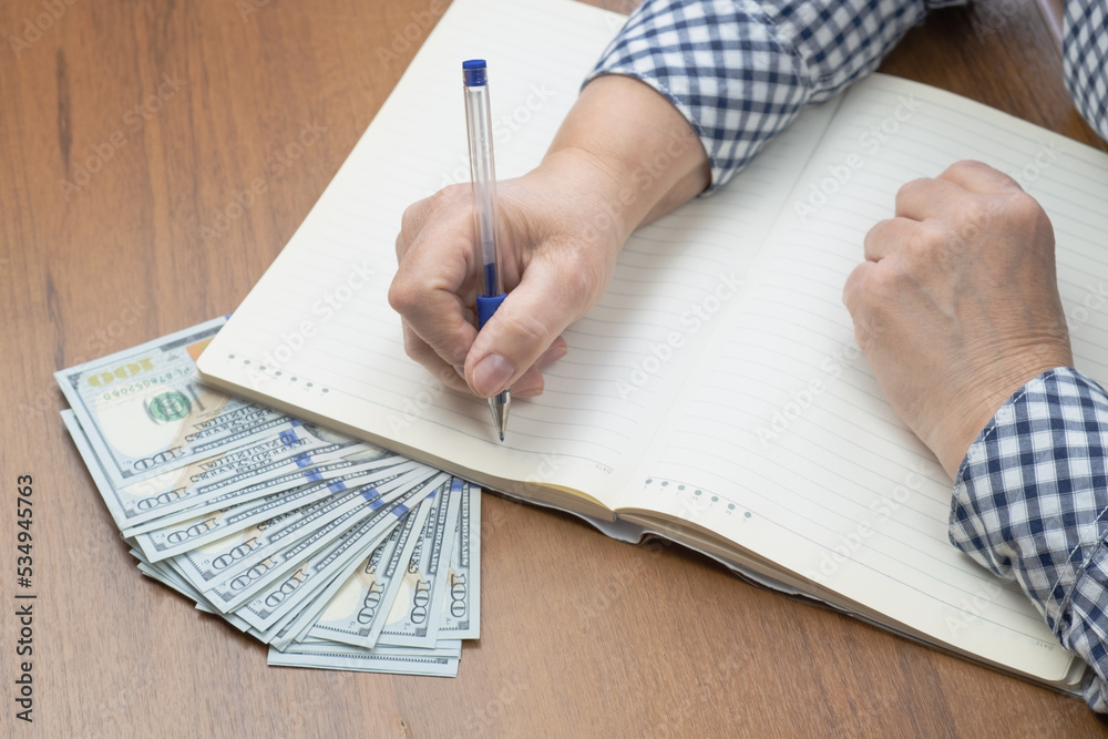 Woman with a notebook, a pen and a stack of cash one hundred dollar ...