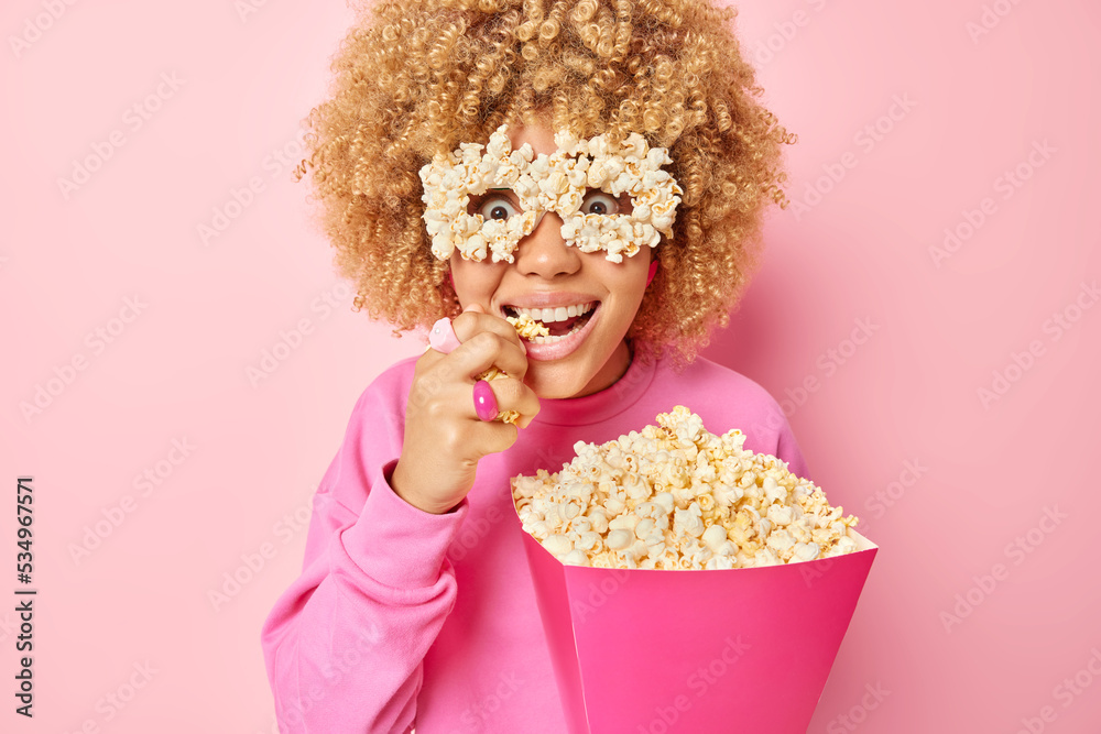 Indoor shot of surprised curly haired woman grabs delicious popcorn ...
