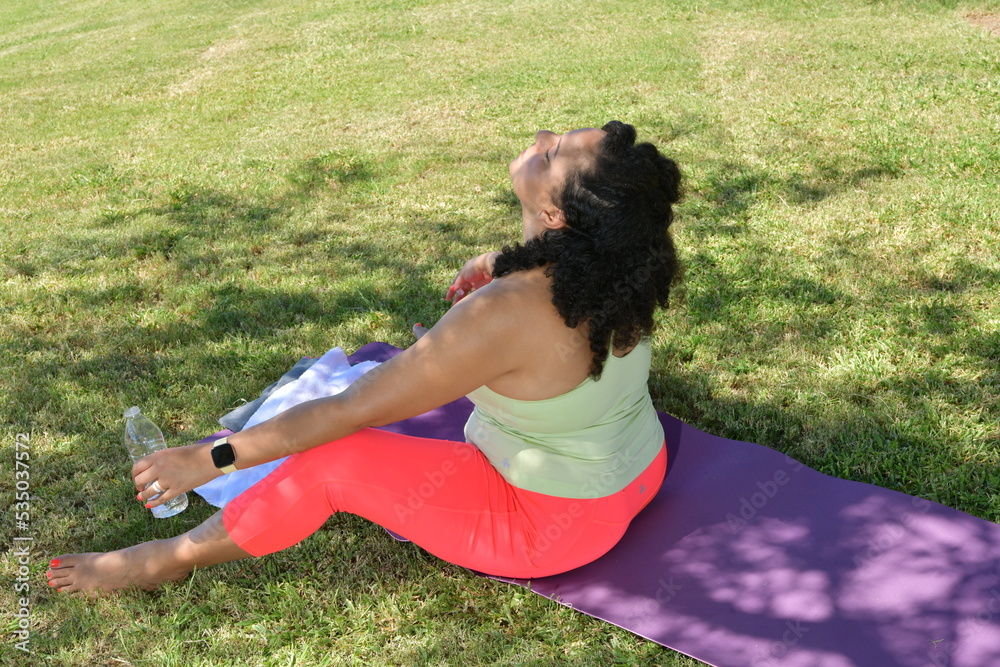 Wavy haired Lady in the park stretching and doing yoga poses on a mat ...