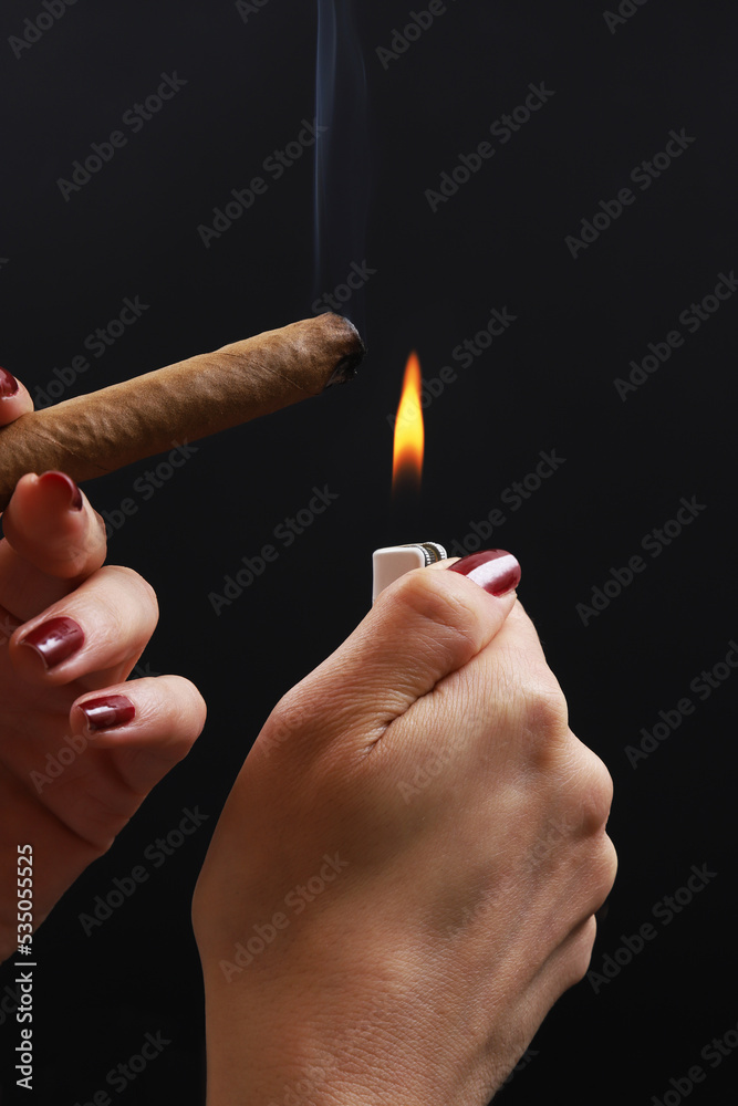 lighter with a spark and a cigar in female hands on a black background ...