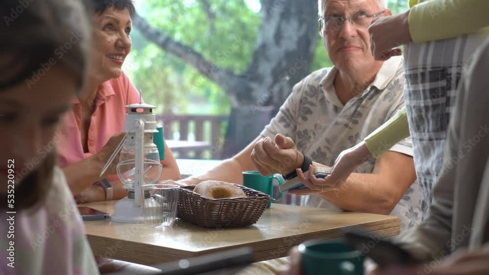 An elder man pay the bill with smart watch wirelessly on POS terminal ...
