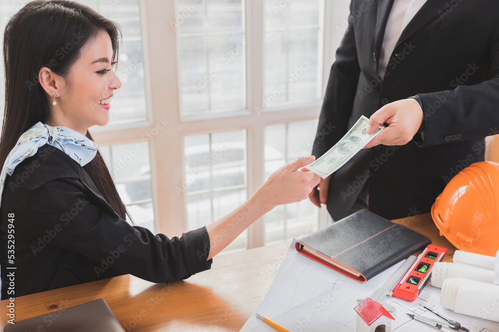 Man offering batch of hundred dollar bills to female architect ...