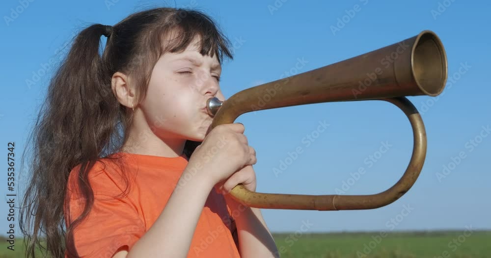 A child with a bugle. Happy little girl blows into the pipe against the ...