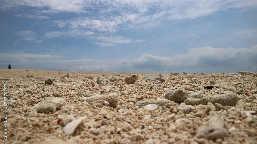 Sand and rocks by the beach against a backdrop of blue sky and soft ...