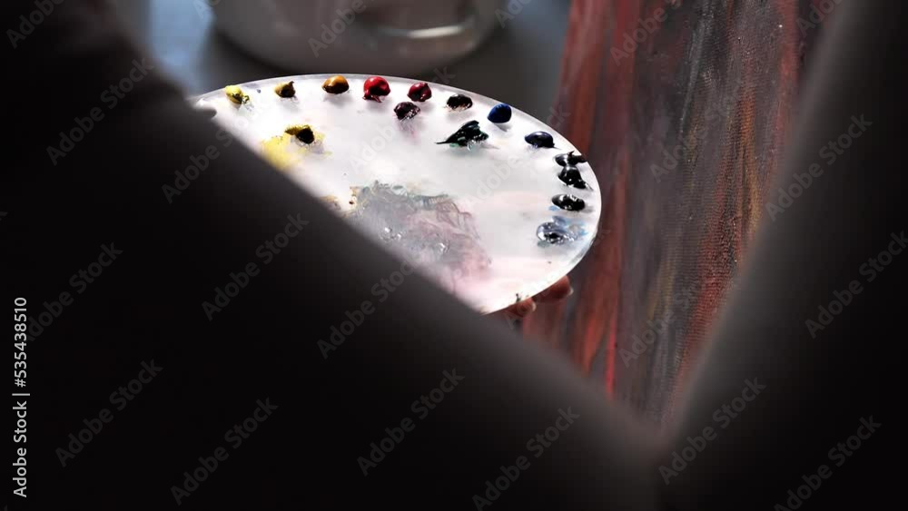 female artist with brush mixes paint in palette while drawing picture ...