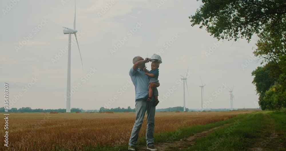 A wind turbine engineer father holds his little son in his arms at a ...
