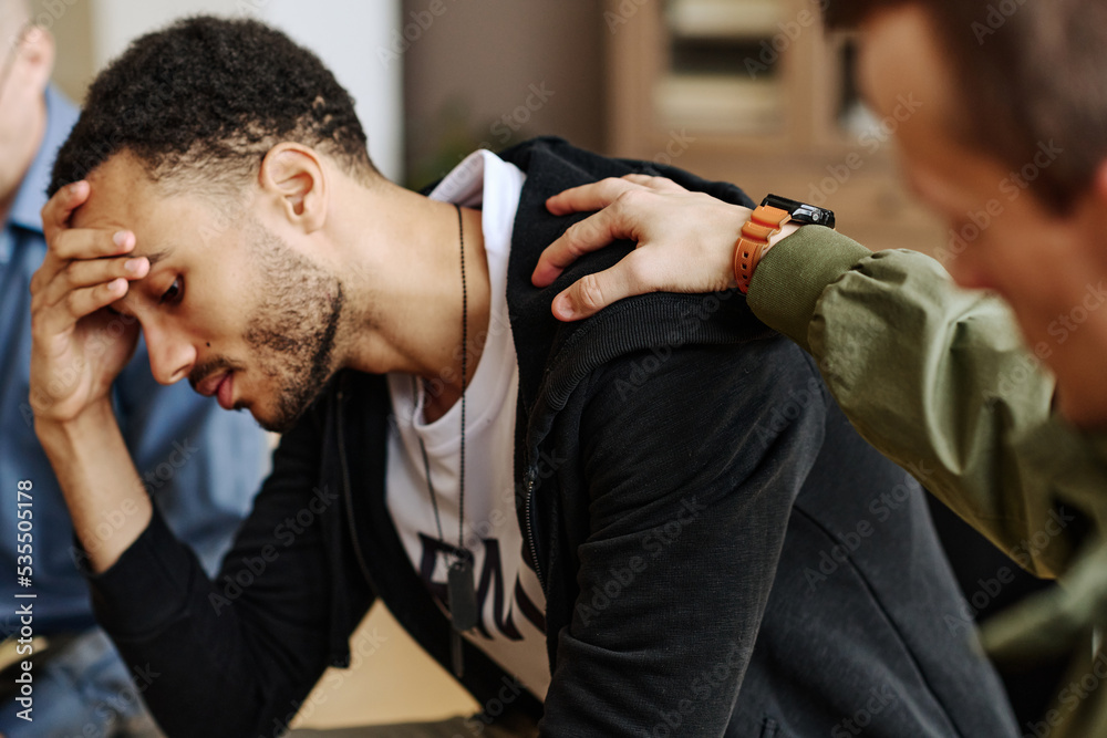 Young stressed man touching head while one of attendants keeping hand ...