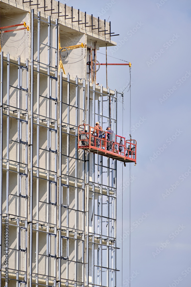 Foto de Suspended construction cradle on white facade of building with ...