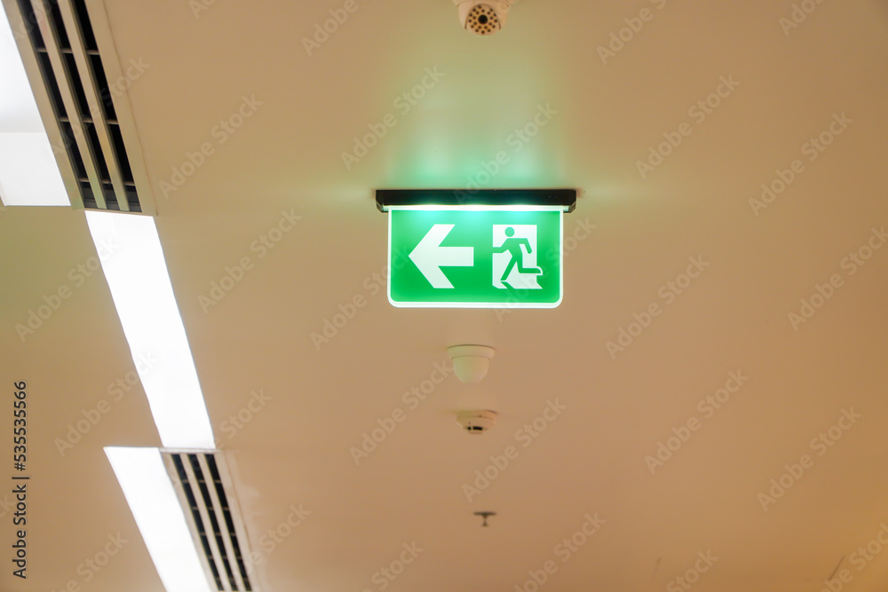 Arrow light box sign of EMERGENCY FIRE EXIT is hung on the ceiling in ...
