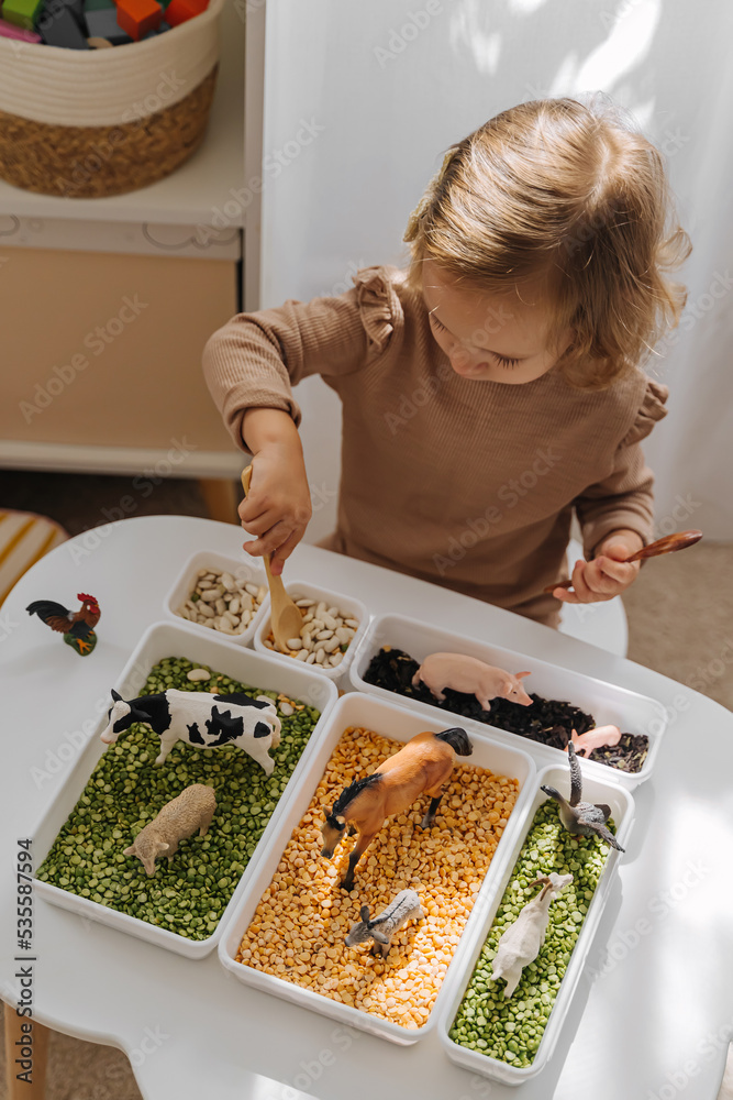 A little girl playing with farm animals in sensory bin in nursery ...