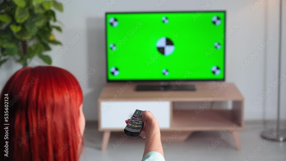 woman changes channels on remote control during space of TV at home ...