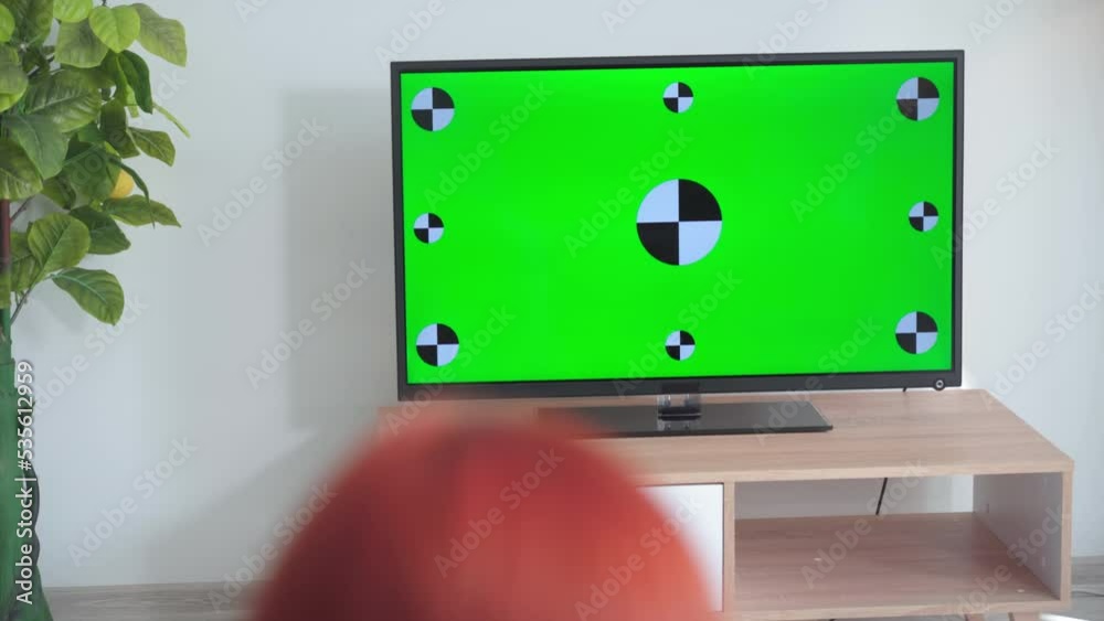 young housewife with remote control switches TV channels on tv with ...