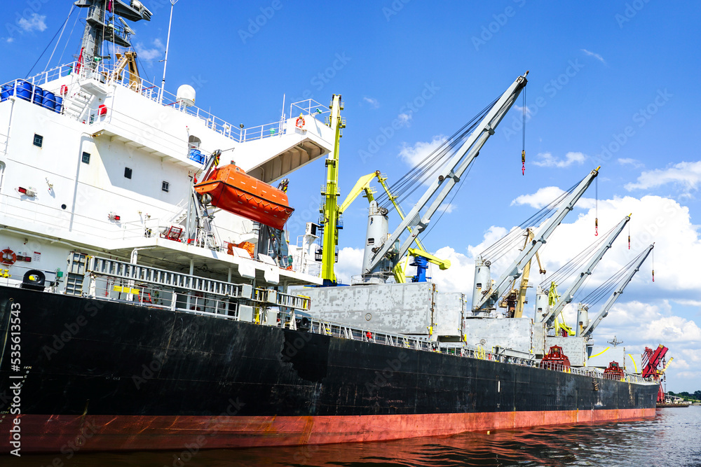 Large bulk cargo ship with open holds in the port cargo terminal, blue ...