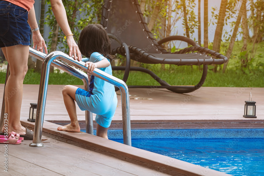 Adorable daughter in blue swimming suit going down swimming pool ladder ...