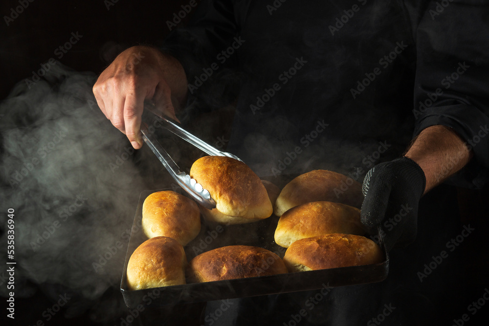 Oven baked buns on a hot baking sheet in the chef hand in glove. The ...