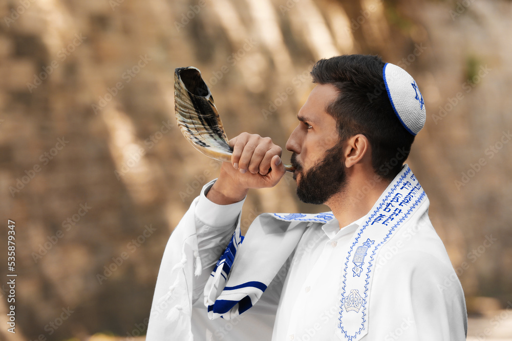 Jewish man blowing shofar on Rosh Hashanah outdoors. Wearing tallit ...