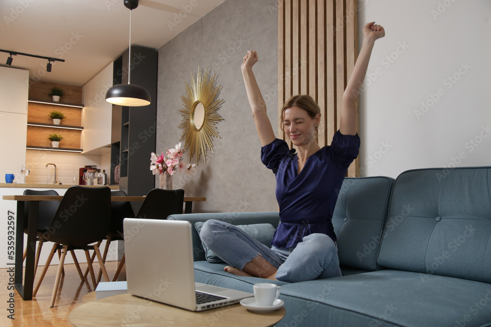 Happy excited woman raising her arms while working on her laptop in the ...