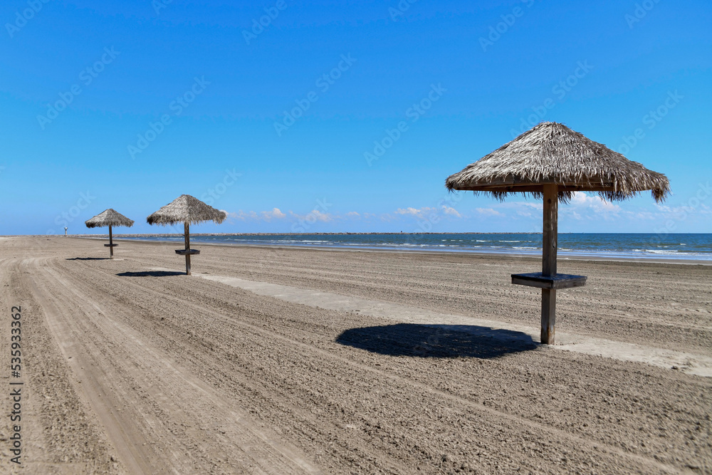 palapas on a deserted, empty beach with surf and a jetty in the ...