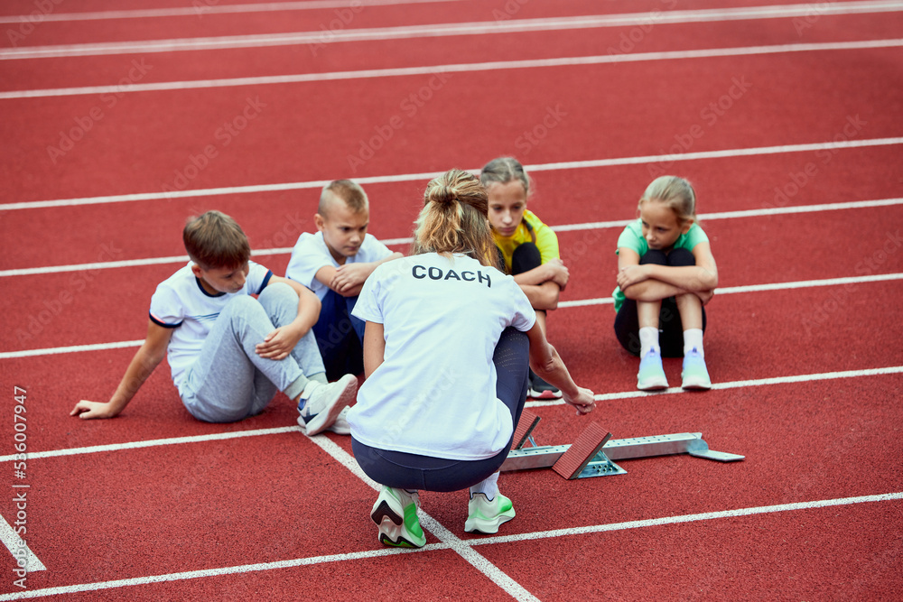 Female coach training athletes. Group of children running on treadmill ...