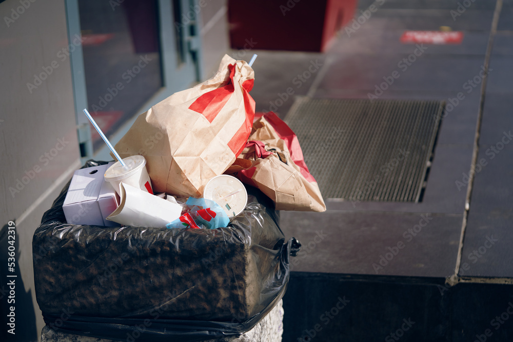 Concrete trash can with black bag inside. Bunch of paper packets and ...