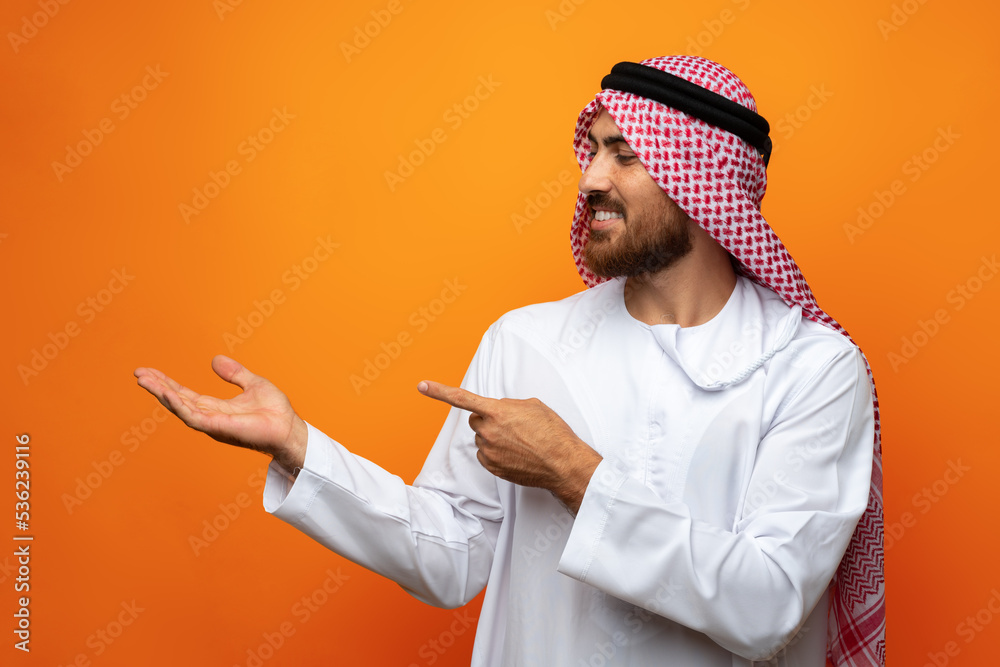Young Arab man pointing hand to copy space on orange background Stock ...