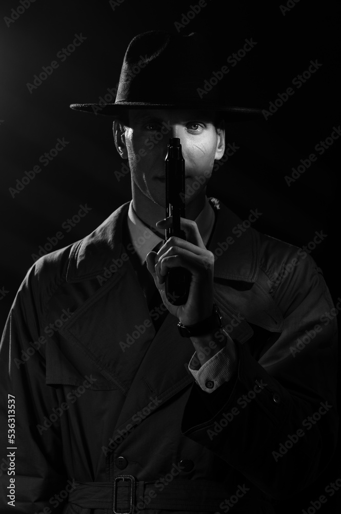 A dark silhouette of a male detective in a coat and hat with a gun at ...