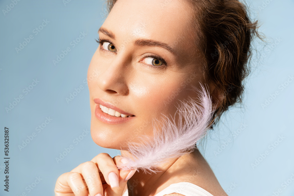 Smiling real woman holding white feather swipes a white feather across ...
