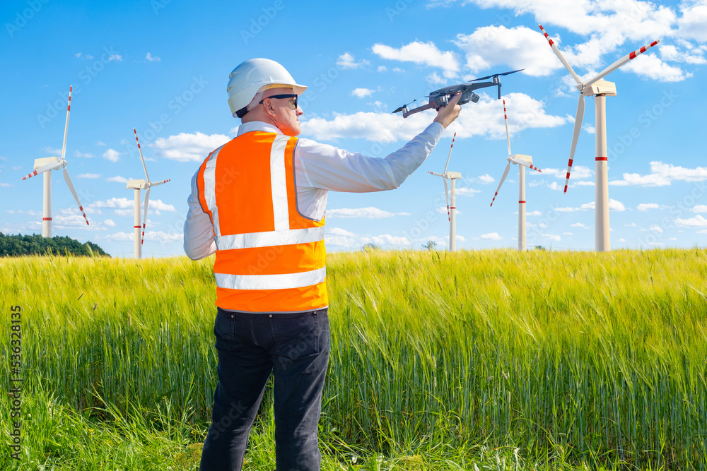 Wind farm engineer. Man with quadcopter and wind turbines. Man launches ...